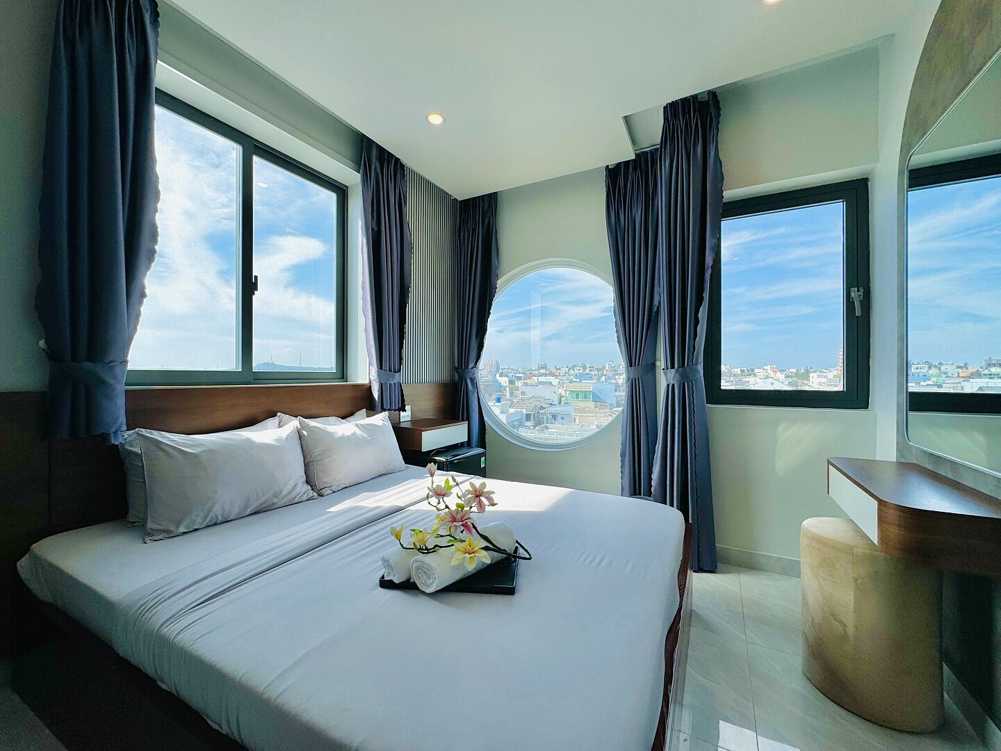 Quarto de hotel moderno com uma cama grande, uma janela redonda e uma escrivaninha.