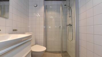 Casa de banho moderna com sanita branca, cabine de duche com vidro e lavatório branco.