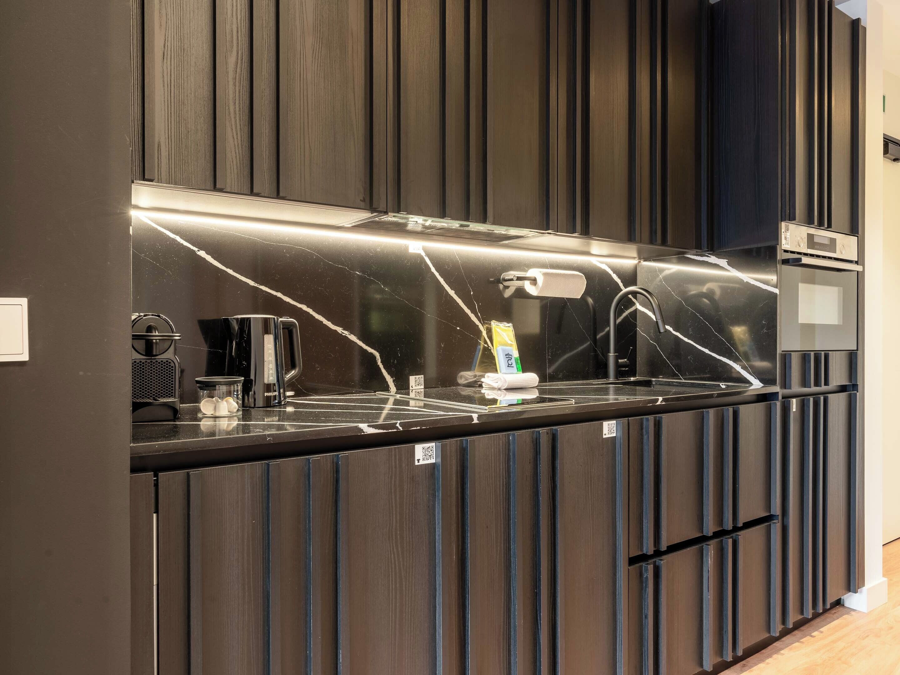 Uma cozinha moderna com bancada de mármore preto, máquina de café integrada e chaleira.