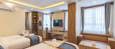 Quarto de hotel com duas camas, uma escrivaninha, televisão, sofá e janela com cortinas.