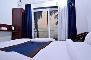 Quarto de hotel com cama, escrivaninha, cadeira, luminária e vista para o oceano ao pôr do sol.