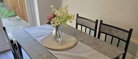 Uma mesa de jantar com um jogo americano, um vaso com flores e cadeiras.