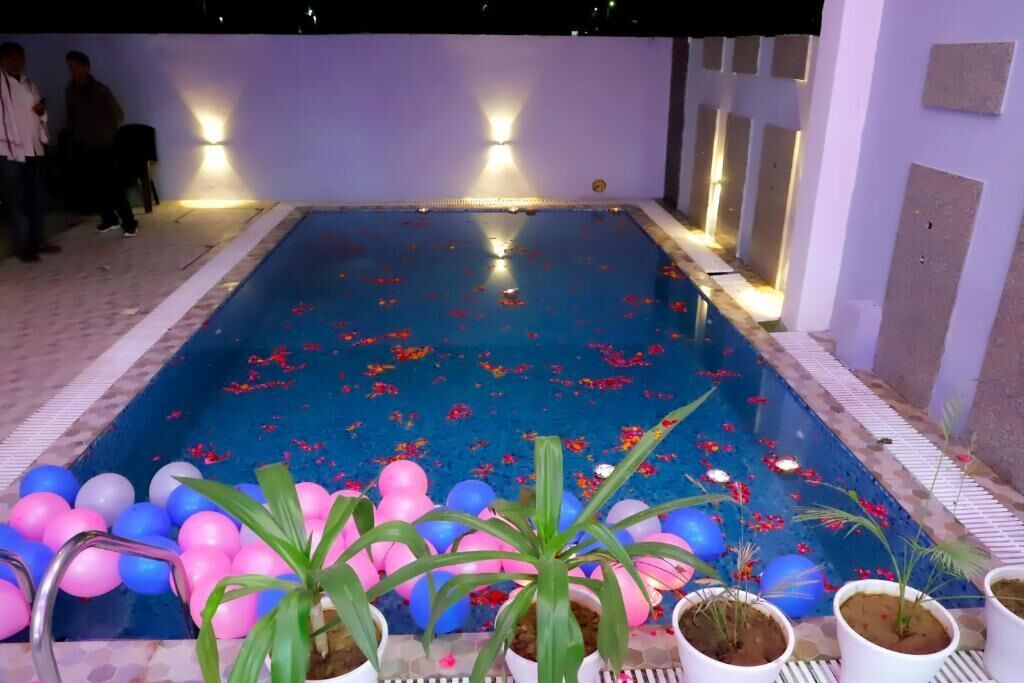 Uma piscina com vitórias-régias e balões, rodeada por plantas em vasos.