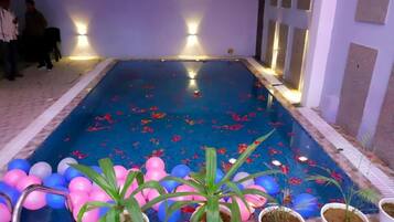 Uma piscina com vitórias-régias e balões, rodeada por plantas em vasos.