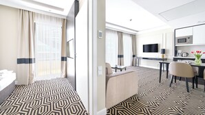 Quarto de hotel com sofá, mesa de jantar, televisão e cozinha equipada com micro-ondas.