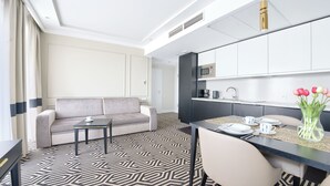 Quarto de hotel moderno com sofá, uma mesinha com uma chávena, zona de refeições com um vaso de tulipas e cozinha com micro-ondas.
