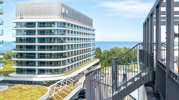 Um edifício moderno de vários andares com fachada curva, grandes janelas e vista para o mar.