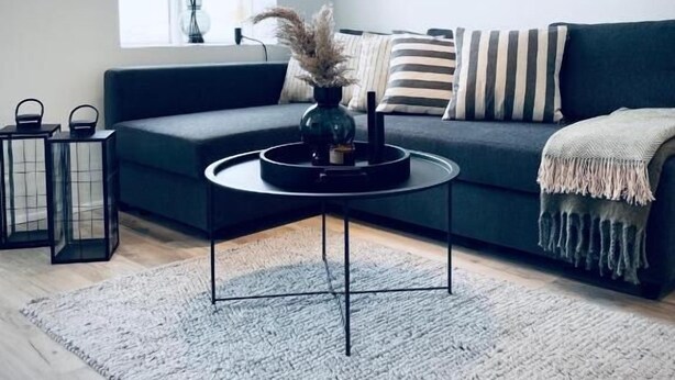 Uma sala de estar moderna com um sofá escuro, uma mesa de centro redonda e uma janela grande.