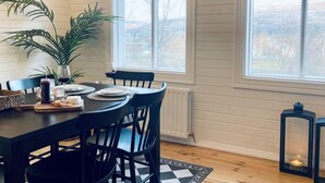Uma sala de jantar com um tapete quadriculado em preto e branco, um lustre e vista para o exterior através de grandes janelas.