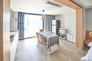 Quarto de hotel moderno com área de refeições, cozinha compacta e uma grande janela com cortinas.