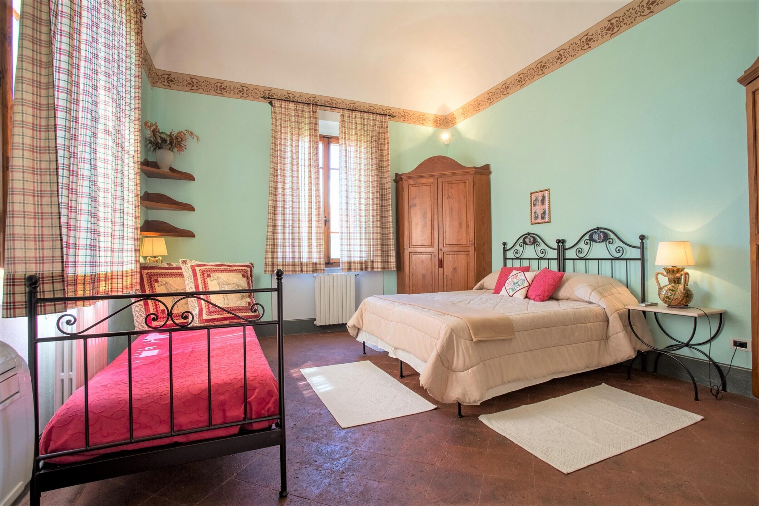 Quarto com cama, mesa de cabeceira, guarda-roupa de madeira e janela com cortinas.