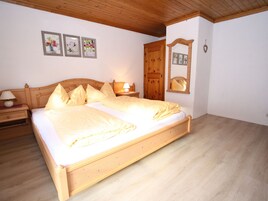 Quarto com cama de madeira, mesa de cabeceira com abajur, guarda-roupa de madeira e três quadros na parede.