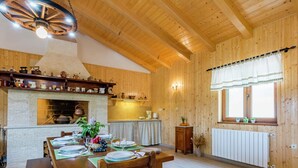 Interior em madeira com mesa de jantar posta para quatro, área de cozinha com fogão e janela com cortinas.