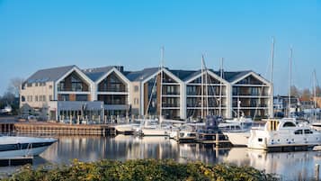 Uma marina com vários barcos atracados, um edifício moderno com grandes janelas e céu claro.