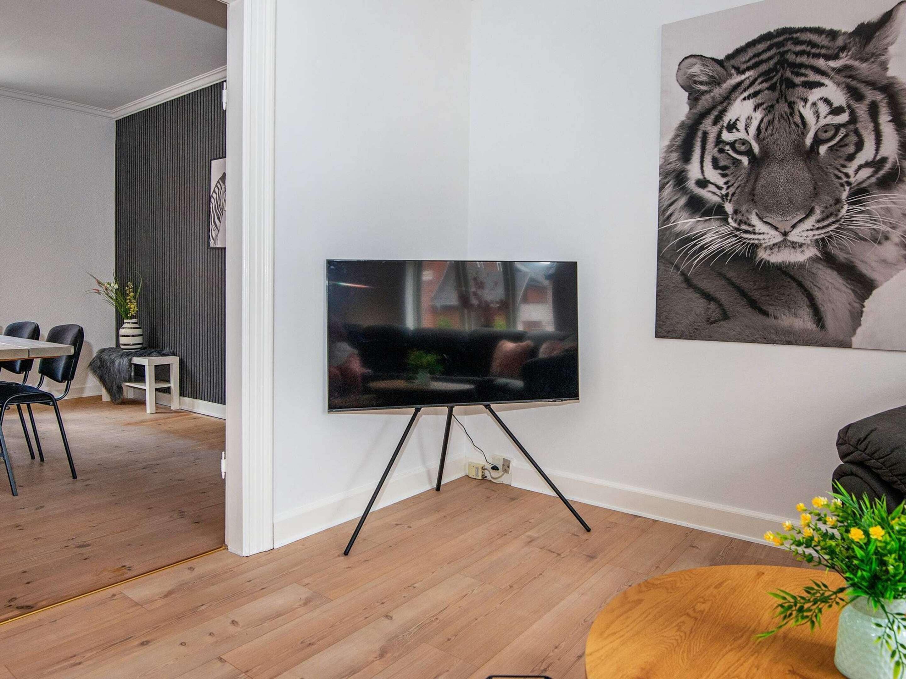 Uma sala de estar moderna com uma TV de tela plana em um suporte, uma grande estampa de tigre na parede e uma área de jantar com cadeiras e uma mesa.