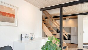 Uma cozinha moderna com eletrodomésticos de aço inoxidável, escada de madeira e bancada branca com um vaso de planta.