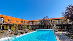 Uma piscina com deck de madeira, cercada por edifícios amarelos com telhados laranja e varandas.