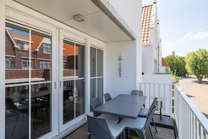 Varanda com mesa e cadeiras, grades brancas e vista para casas vizinhas.