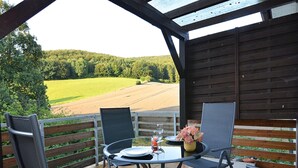 Um pátio externo com uma mesa e cadeiras, com vista para um campo verde.