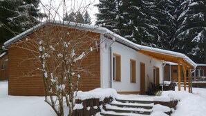 Uma cabana de madeira com varanda, rodeada por árvores cobertas de neve.