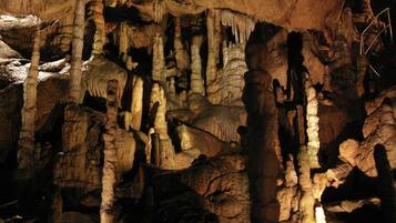 Caverna com estalactites e estalagmites, iluminada por luz artificial.