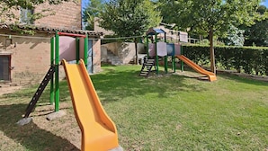 Um parquinho com escorregadores e estruturas de escalada, cercado por gramado e árvores.
