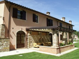 Uma casa de dois andares com fachada de pedra, um alpendre coberto com móveis de exterior e um portão de entrada.