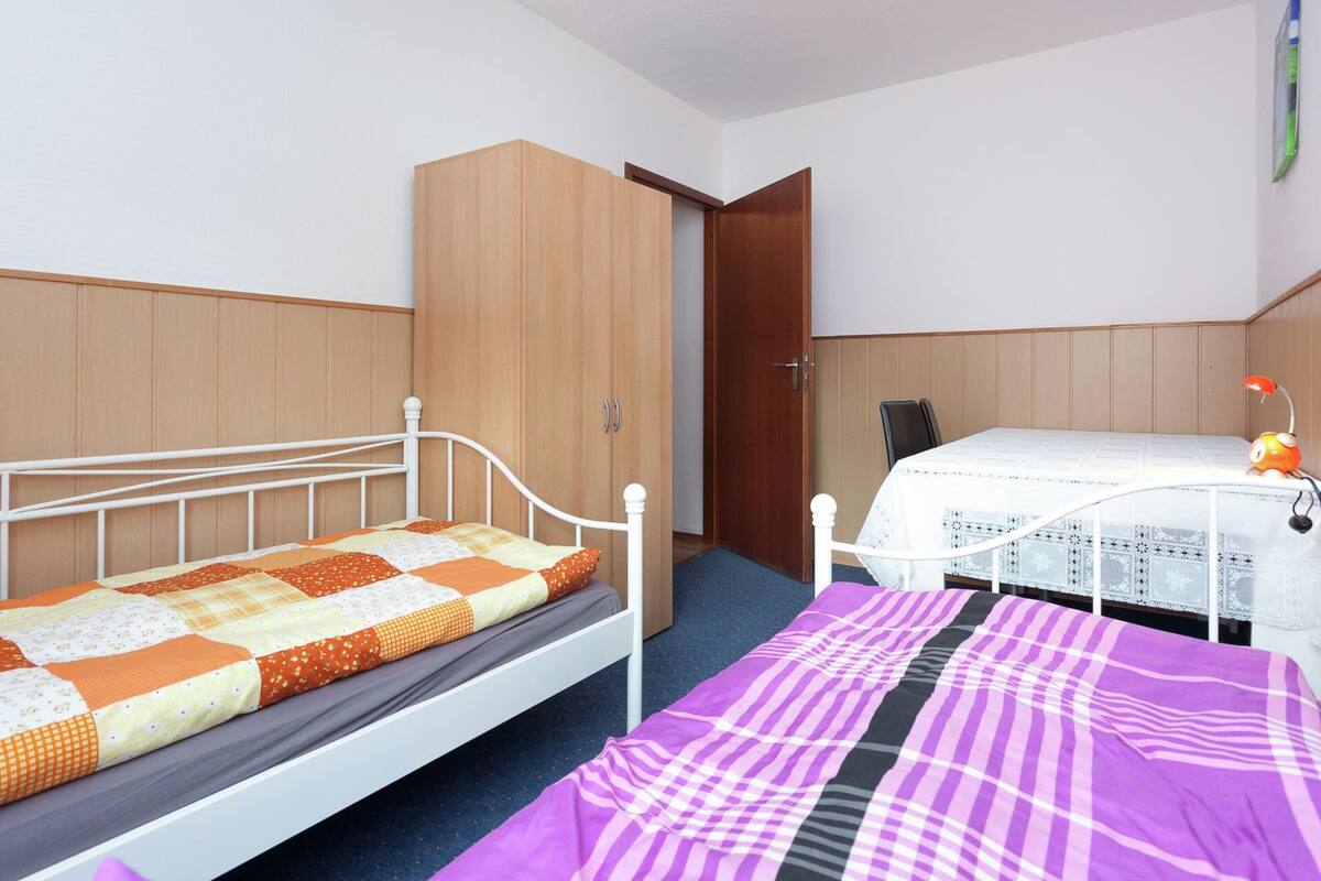 Quarto com duas camas, um guarda-roupa de madeira e uma pequena mesa com abajur.