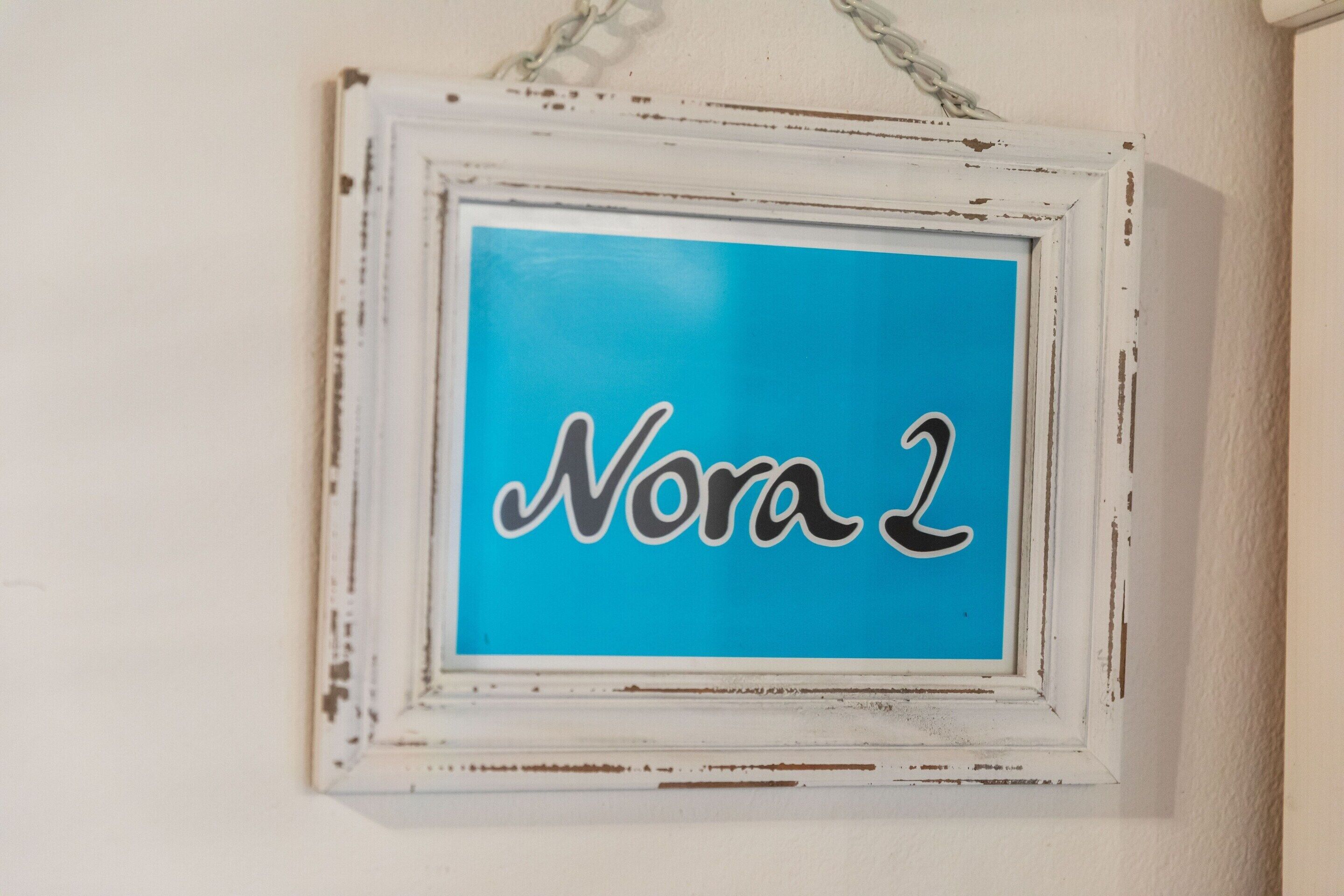 Uma placa emoldurada com o texto 'Nora 2' sobre um fundo azul.