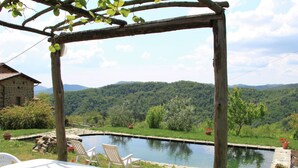Uma área de estar rústica ao ar livre, com mesa e cadeiras, com vista para um lago calmo e colinas verdes exuberantes.