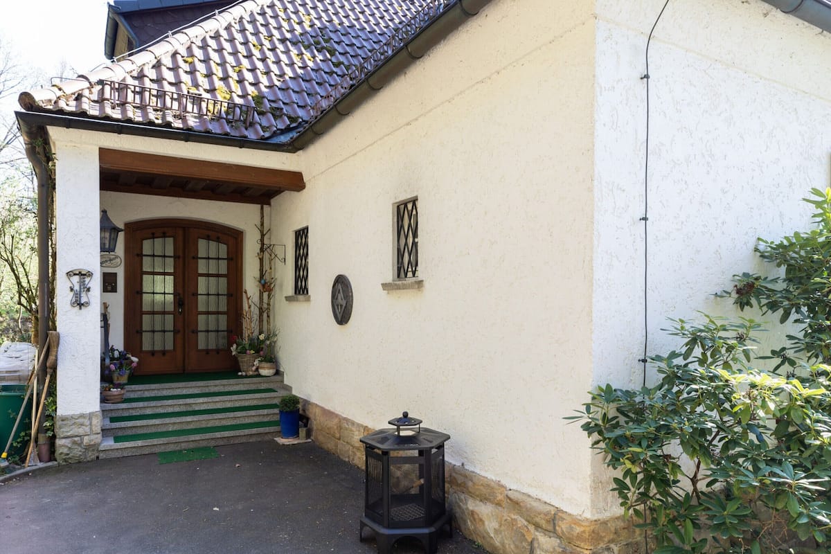 Um edifício com telhado de telhas, porta de madeira e um pequeno espaço ao ar livre com mesa e lanterna.