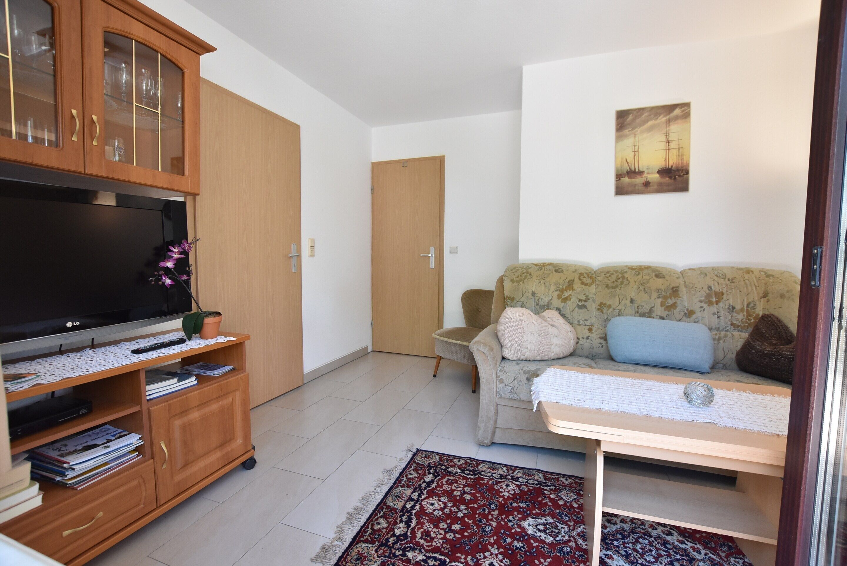 Uma sala de estar com televisão, aparador de madeira, sofá e um quadro na parede.