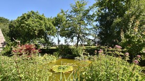 Um jardim tranquilo com lago, vegetação exuberante e plantas floridas.