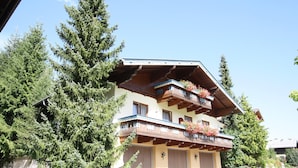 Um edifício com várias andares e varandas, rodeado por altas árvores perenes.