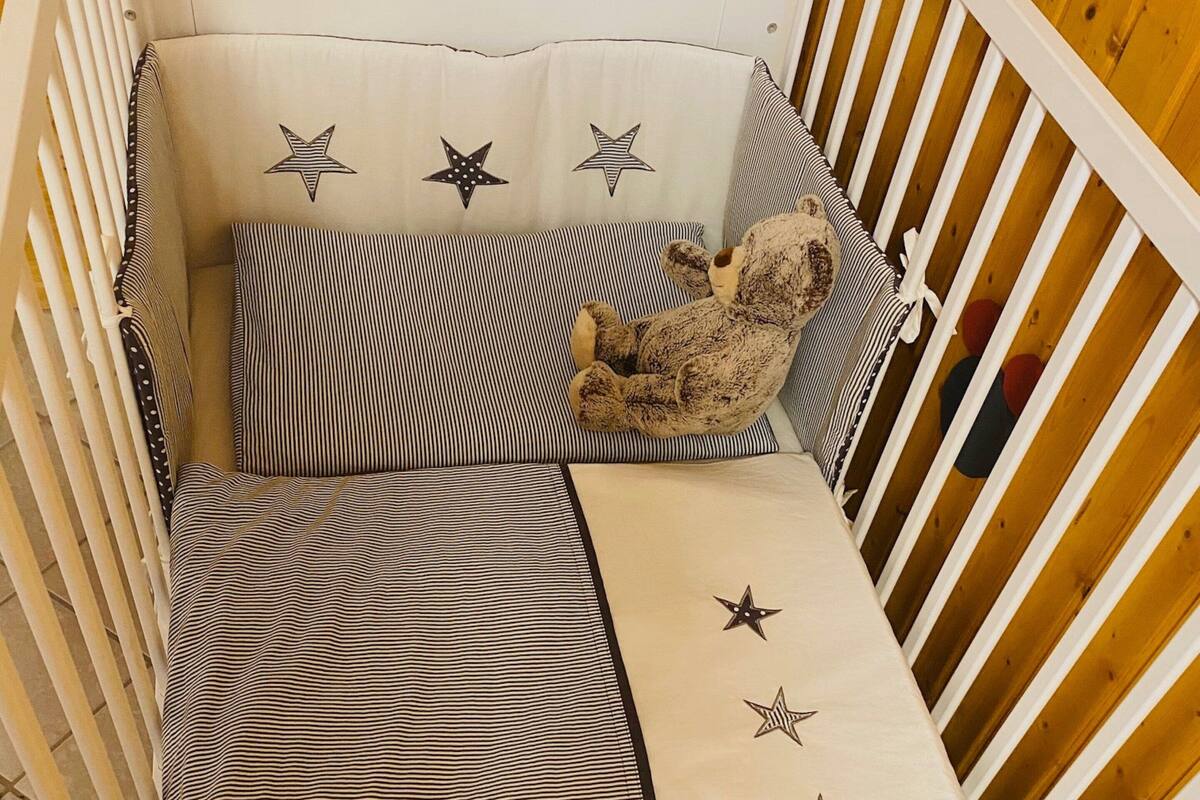 Berço com colchão e travesseiros listrados, um urso de pelúcia e um cobertor estampado com estrelas.