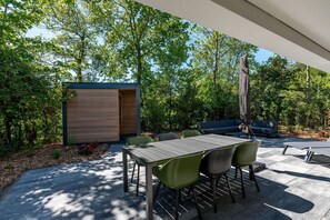 Um pátio externo com mesa e cadeiras, cercado por vegetação e uma estrutura de madeira.