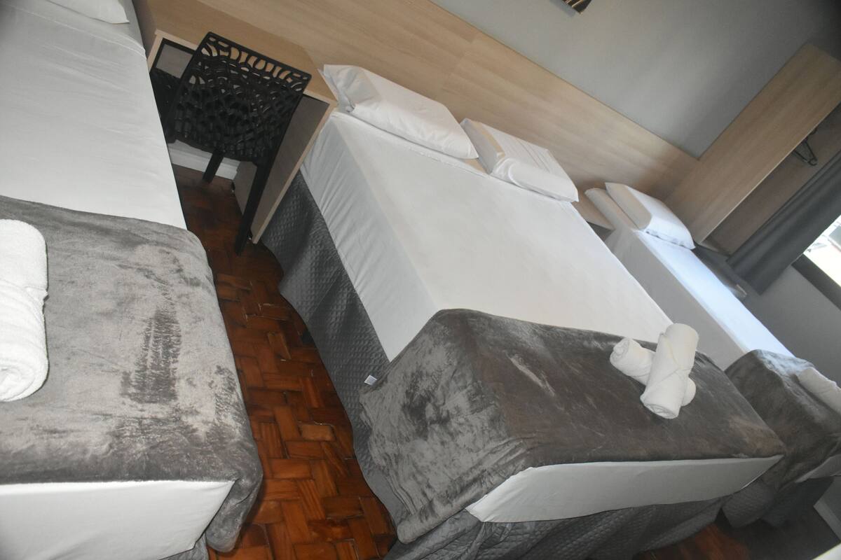 Quarto de hotel com duas camas, piso de madeira e janela com cortinas.