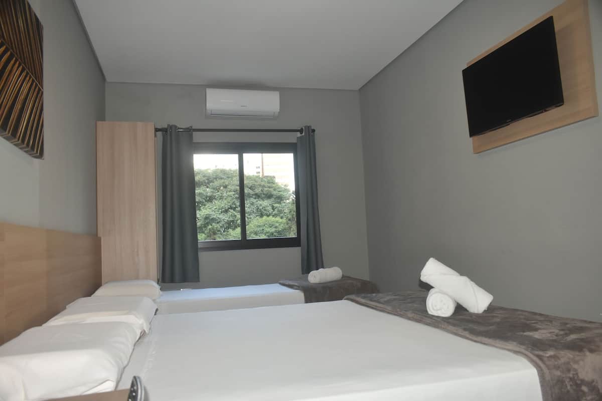 Quarto de hotel com duas camas, janela com cortinas, TV de tela plana na parede e ar-condicionado.