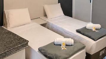 Quarto com duas camas, um pequeno espaço de cozinha e uma porta.