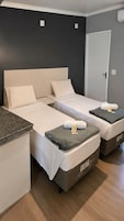 Quarto com duas camas, um pequeno espaço de cozinha e uma porta.