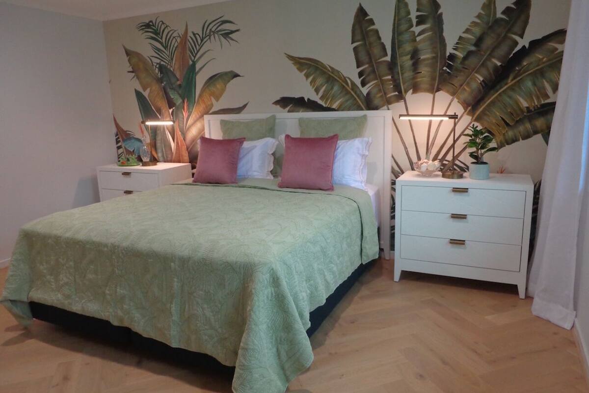 Quarto com cama, mesas de cabeceira e uma planta grande.