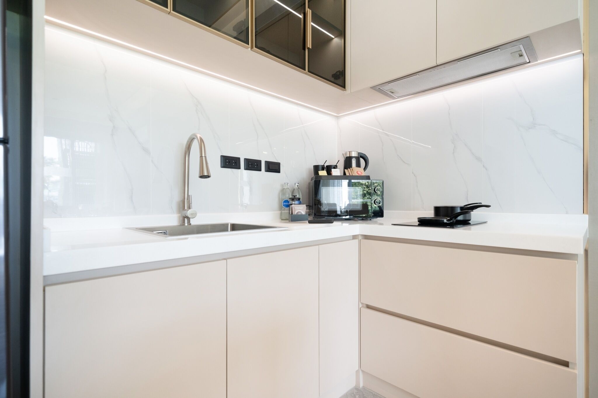 Uma cozinha moderna com bancadas de mármore branco, uma torneira de aço inoxidável e uma máquina de café.