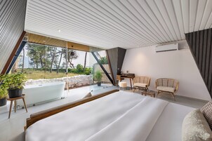 Quarto moderno com uma cama grande, banheira de vidro e cadeiras de vime, com vista para o exterior.
