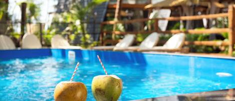 Área de piscina com espreguiçadeiras e dois cocos com canudos.