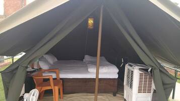 Uma tenda com uma cama, um ventilador e uma mesa.