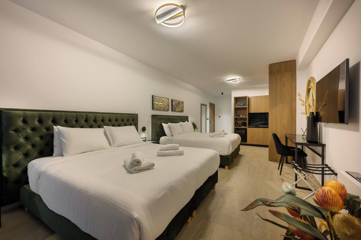 Quarto de hotel com duas camas, uma escrivaninha e uma cozinha compacta.