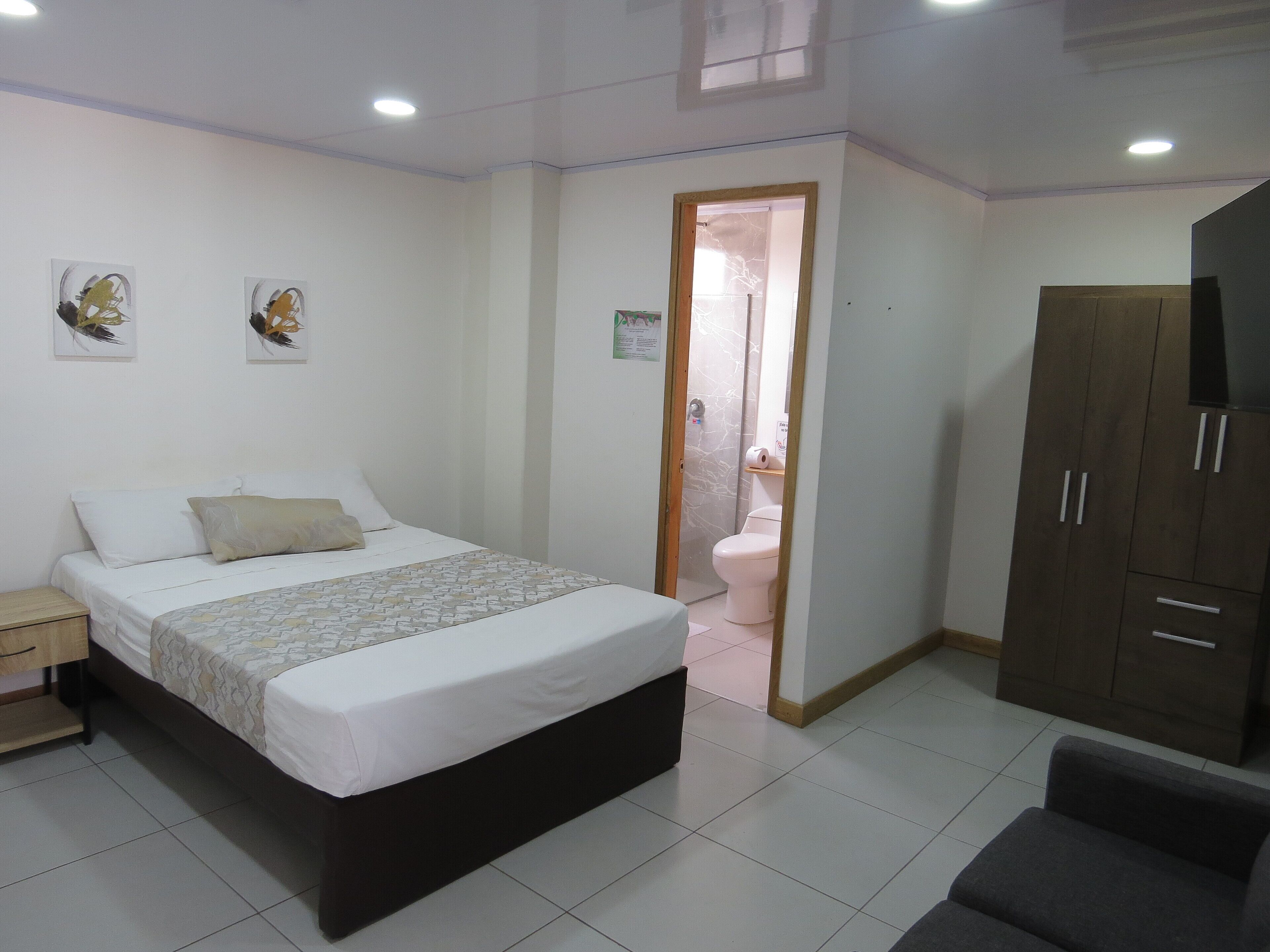 Quarto com cama, guarda-roupa e banheiro visível por uma porta aberta.