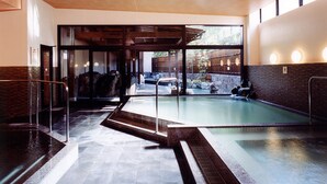 Piscina interna com piso de pedra, paredes de vidro e teto de madeira.