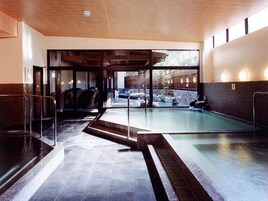 Piscina interna com piso de pedra, paredes de vidro e teto de madeira.