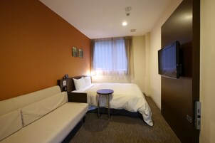 Quarto de hotel com cama, sofá, mesinha, televisão e janela com cortinas.